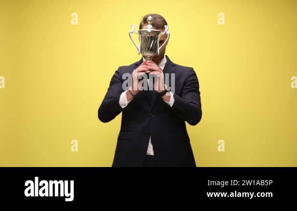 goofy young businessman hiding behind silver trophy, looking over ...