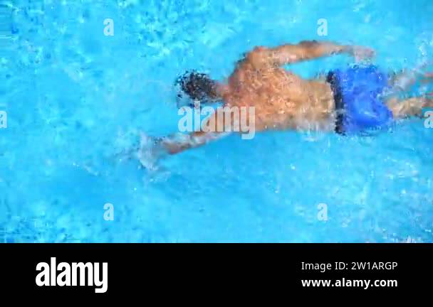 Muscular man swimming through pool splashing water. Young sporty guy ...