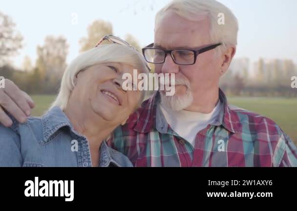Close-up portrait of a happy Caucasian retired family sitting on the bench in sunlight and ...