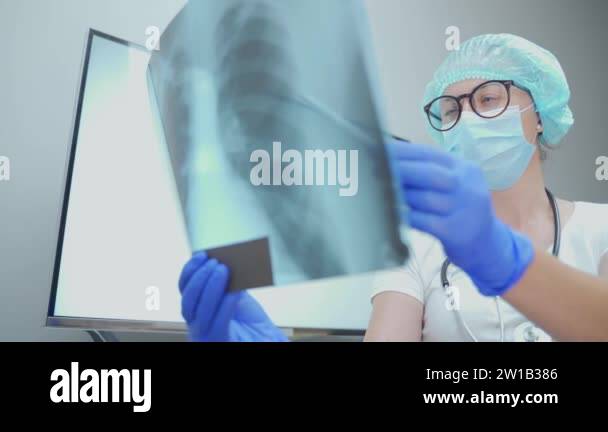 Woman doctor sitting at desk, working on computer, holding X-ray of ...