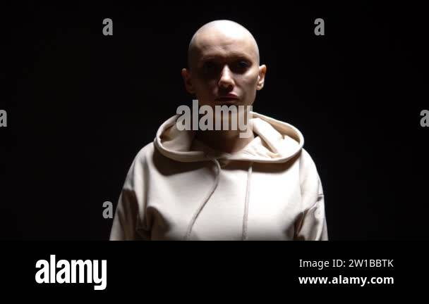 a bald woman looks sadly into the camera, light passes through her face ...