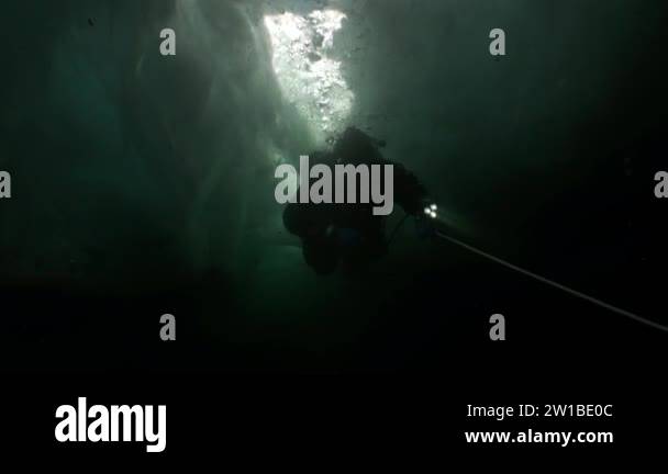 Underwater cameraman with camera and technical diver under ice of lake ...