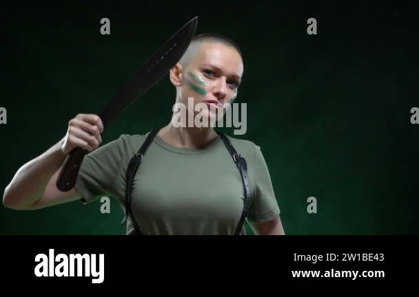 Angry bald girl with camouflage makeup shaving machete hair on a black ...