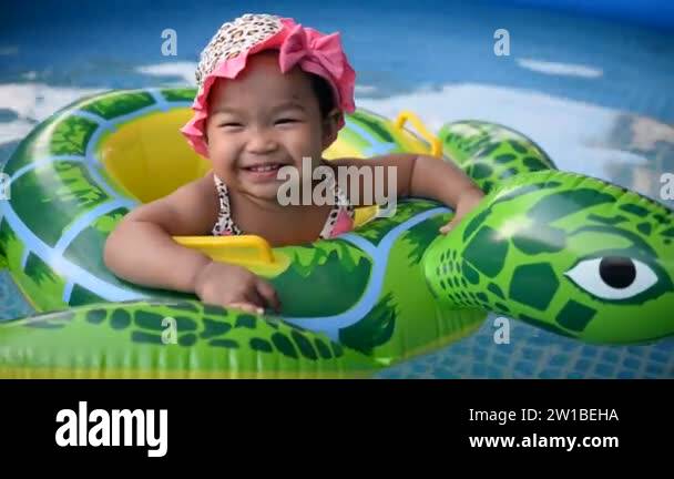 cute Asian little girl in hat floating in inner tube at swimming pool ...