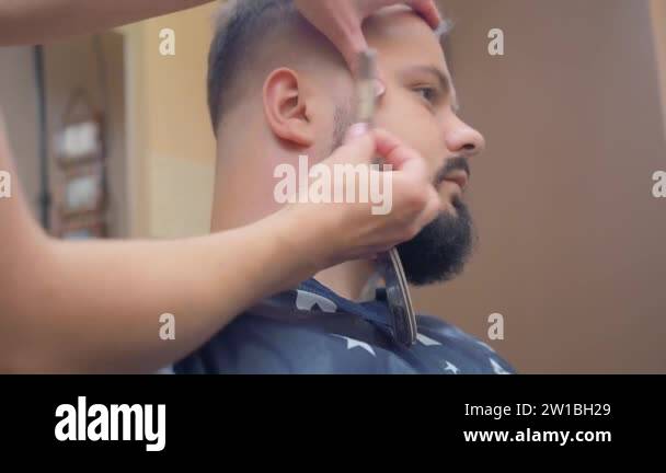 Stylist in dark red dress shaving clients neck with open razor, close ...