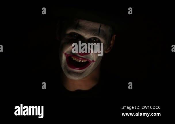 Scary man in a clown makeup looks at the camera and laughs. A scary ...