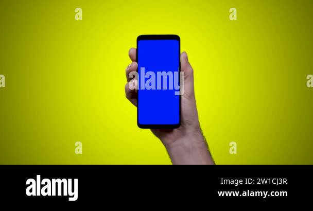 man hand holding smartphone with blue chroma key on yellow background ...