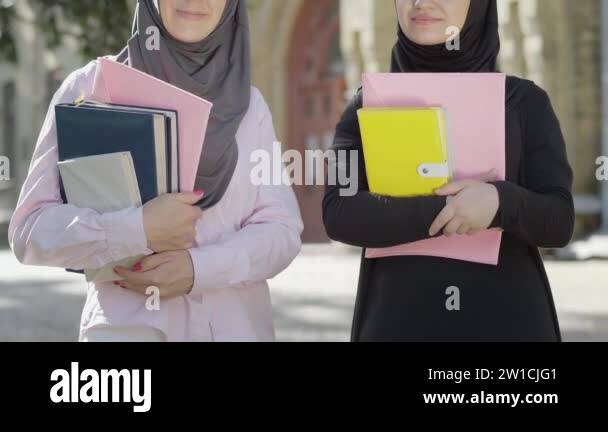 Two unrecognizable Muslim student posing outdoors with book. Front view ...