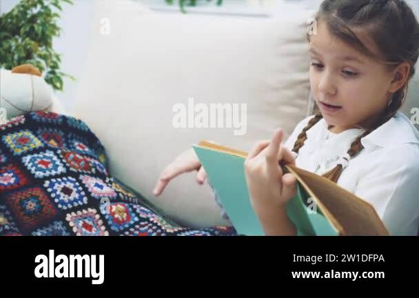Cute little girl sitting with her legs curled up, reading fairy-tale ...