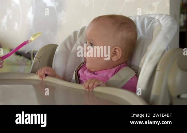 Little cute girl sits behind a children's chair and plays with spoon ...