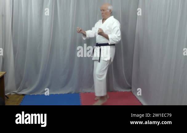 On a red and blue tatami, an old man athlete raises his legs and beats ...