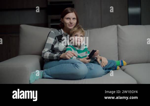 Mother and son sitting on cozy sofa and switching on TV by remote ...