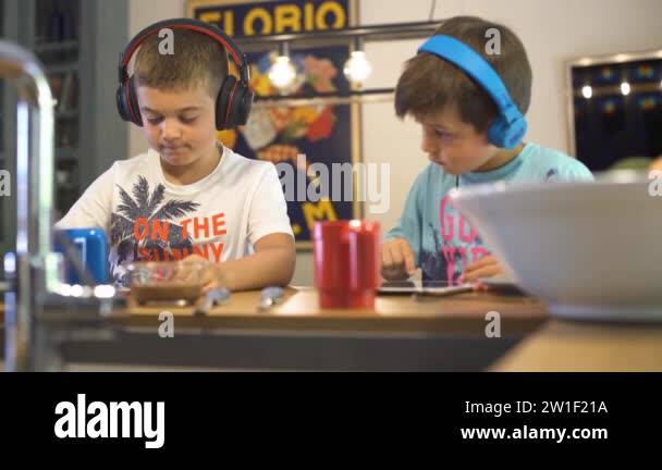 Two children with headphones play with their tablets, and talk about ...