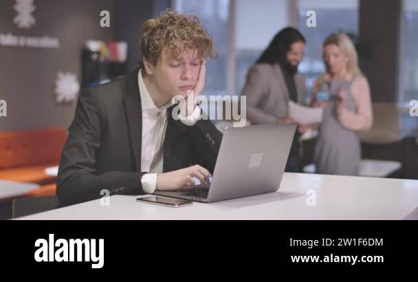 Portrait of tired Caucasian young man typing on laptop keyboard ...
