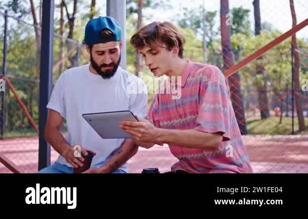 Closeup to the camera two good friends guys in a modern park using a ...