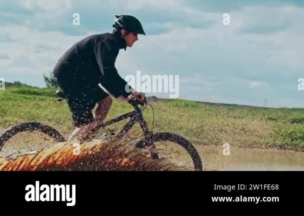 Young man drives into a large puddle on a black mountain bike. Cyclist ...