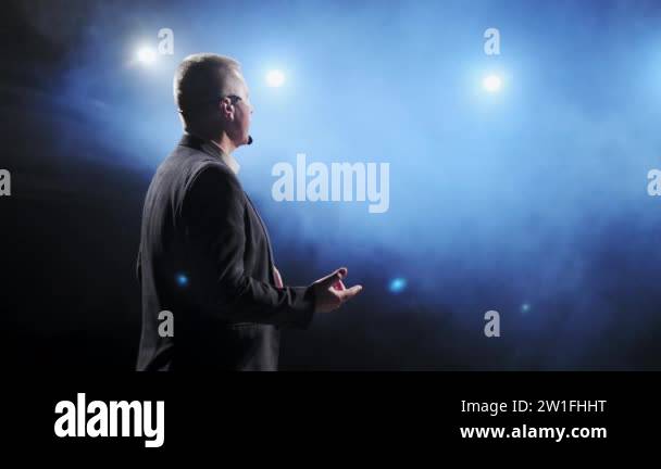 Rear view of men speaking through a microphone in dark conference hall ...