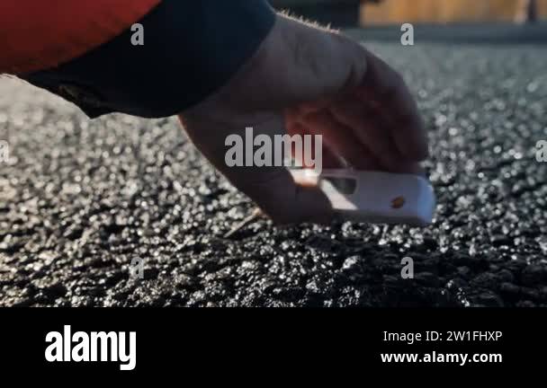 Measuring the temperature of fresh asphalt. Close-up of a mans hand ...