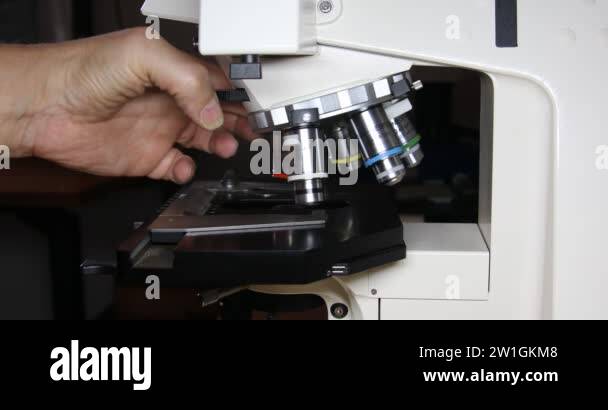 the hand of a scientist turns the microscope revolver with objectives ...