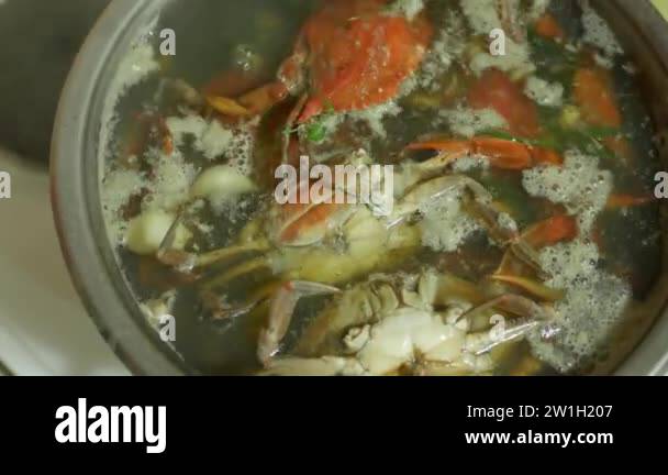 The chef stirs with a spoonful of blue crabs in a saucepan with boiling ...