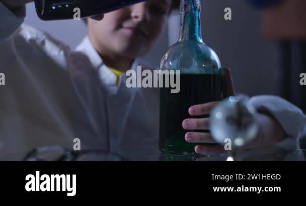 Close-up of liquids in flasks mixed up by Caucasian boy. Curly-haired ...