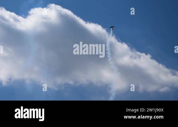 Black plane flies in sky, releasing smoke. Aircraft performs loops at ...