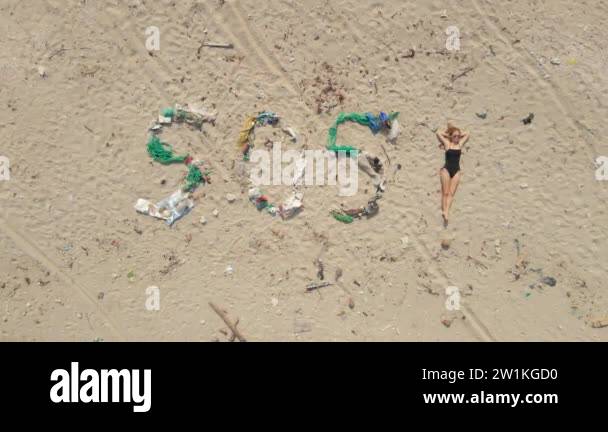Aerial shot of the sign SOS made of trash on a beach. Woman lays by the ...