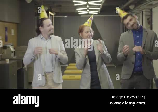 Three Caucasian office workers in party hats dancing in coworking space ...