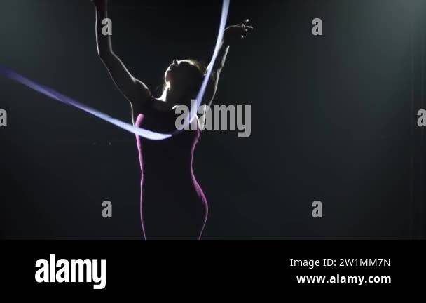 Silhouette of a slim young female gymnast in tight fitting body doing ...