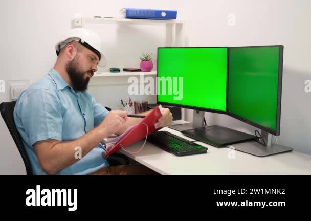 Engineer Wearing Safety Vest and Hardhat Works on a Computer, Two ...