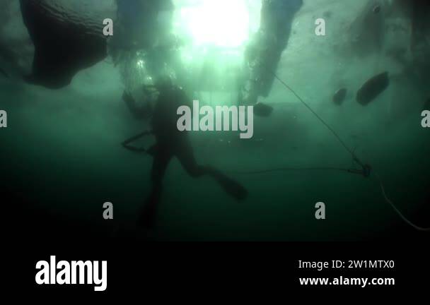 Diving under ice of cameraman underwater diver in cold water of lake ...