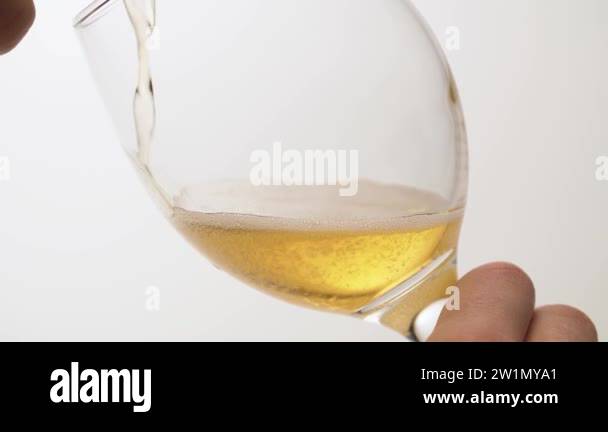 Close up of male hand pouring beer from a bottle into a glass, low angle side view, white ...
