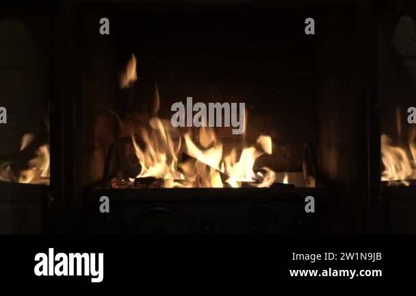 A bright fire inside the fireplace behind glass doors against a brick ...