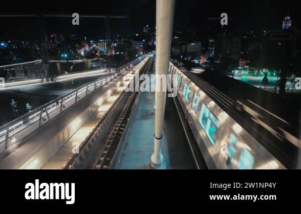 A metro train pulls up to a platform on a bridge overlooking the night city. Public ...