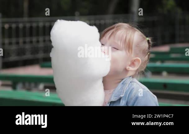 Beautiful and happy little girl eating cotton candy on the bench. Young ...