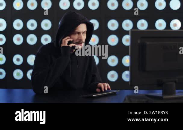 Bearded man computer hacker wearing black hoodie is sitting in modern ...