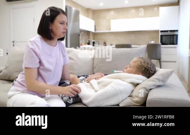 mother caring for sick child lying in bed with flu measuring temperature using thermometer ...