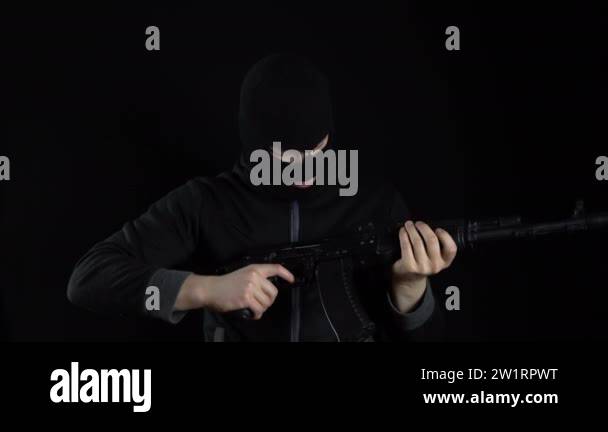 A man in a balaclava mask stands with an AK-47 assault rifle. The ...