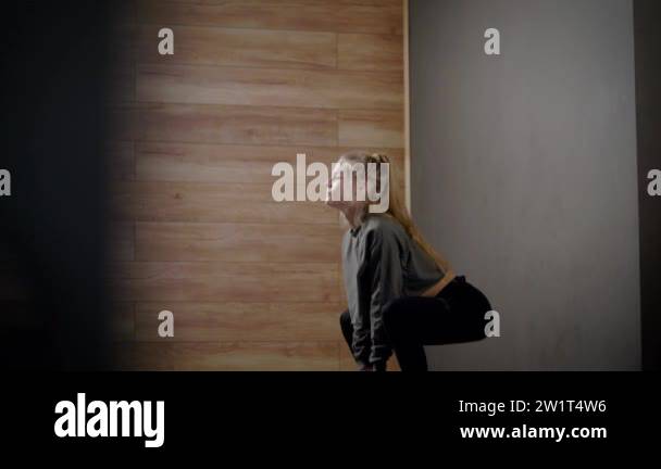 young woman is crouching in fitness hall, holding kettlebell in hands ...