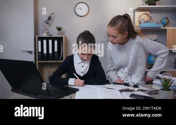 Satisfied teen older girl giving high five to her younger sister while doing together hometask ...