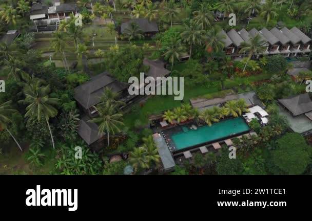 Rising up Aerial view of luxury hotel with straw roof villas and pool in tropical jungle, palm ...