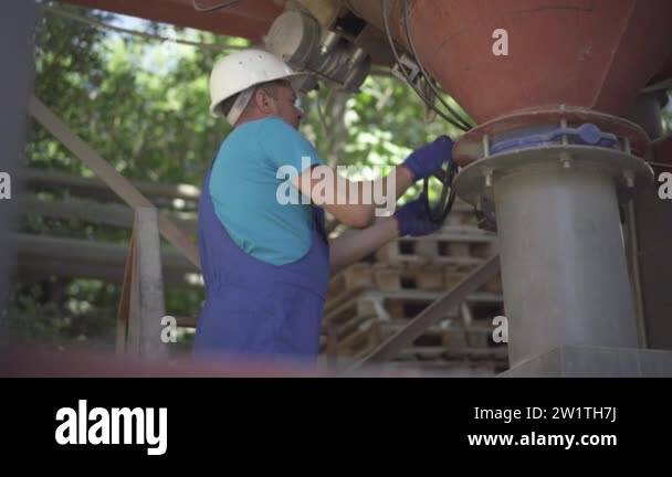 Serious factory worker adjusting industrial equipment on concrete ...