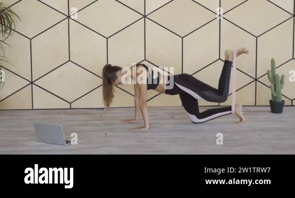 Young sportive woman doing hip exercise at home, shaking leg engaged in ...
