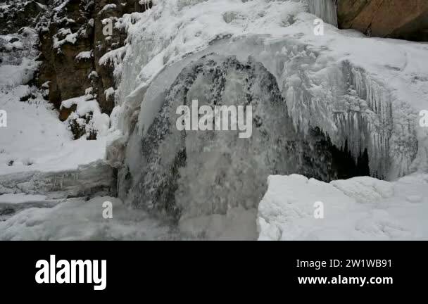 Frozen waterfall in the winter in the mountains. Water flows from under ...