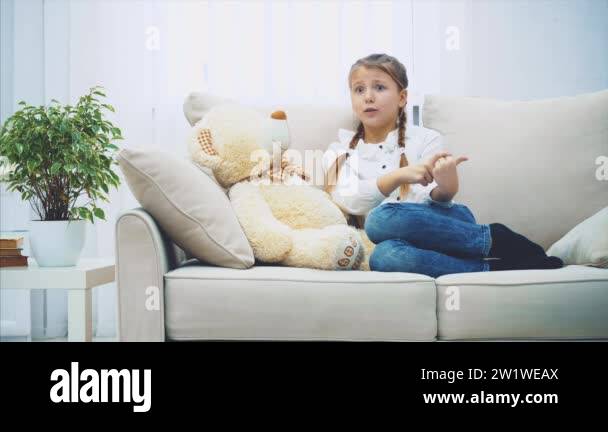 Cute little girl sitting on the sofa, talking with her teddy ...