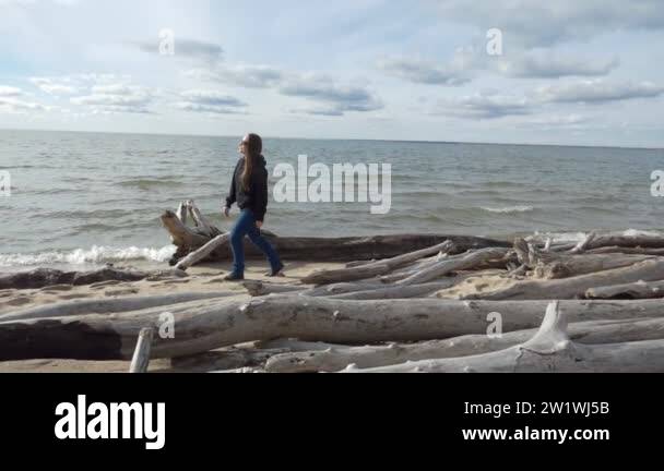 Environment. A young woman walks along the river Bank where tree trunks are brought by the ...