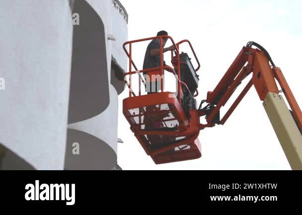 Mature man on a telescopic boom lift platform approaches a wall in to ...