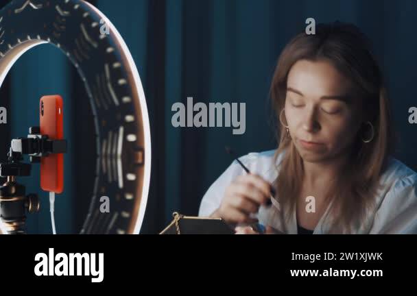 Female vlogger fills in her brows holding mirror in hands in front of ...