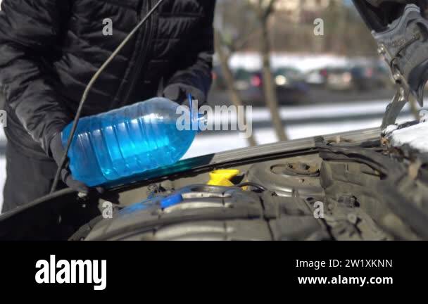Man pouring an antifreeze liquid into a windshield washer tank of a car ...