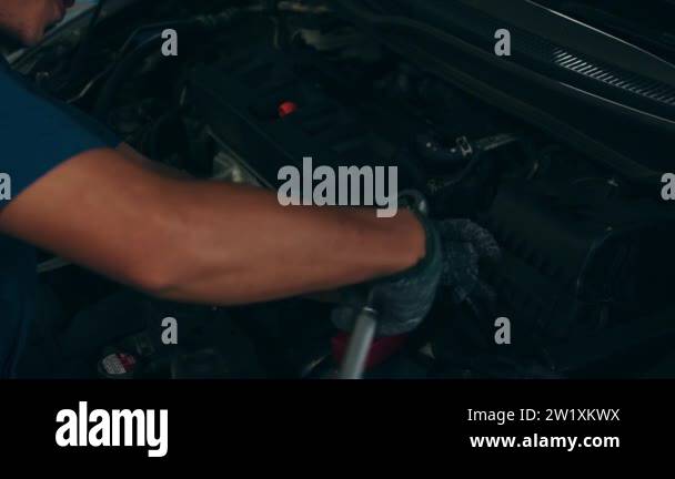 Professional car mechanic screwing details of car engine on lifted ...